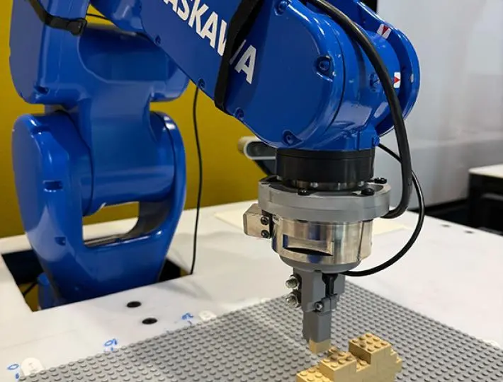 A blue robotic arm builds a figure out of Lego bricks.