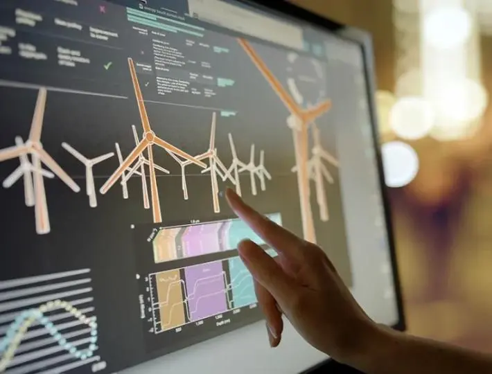 A hand points at images of wind turbines on a computer screen.